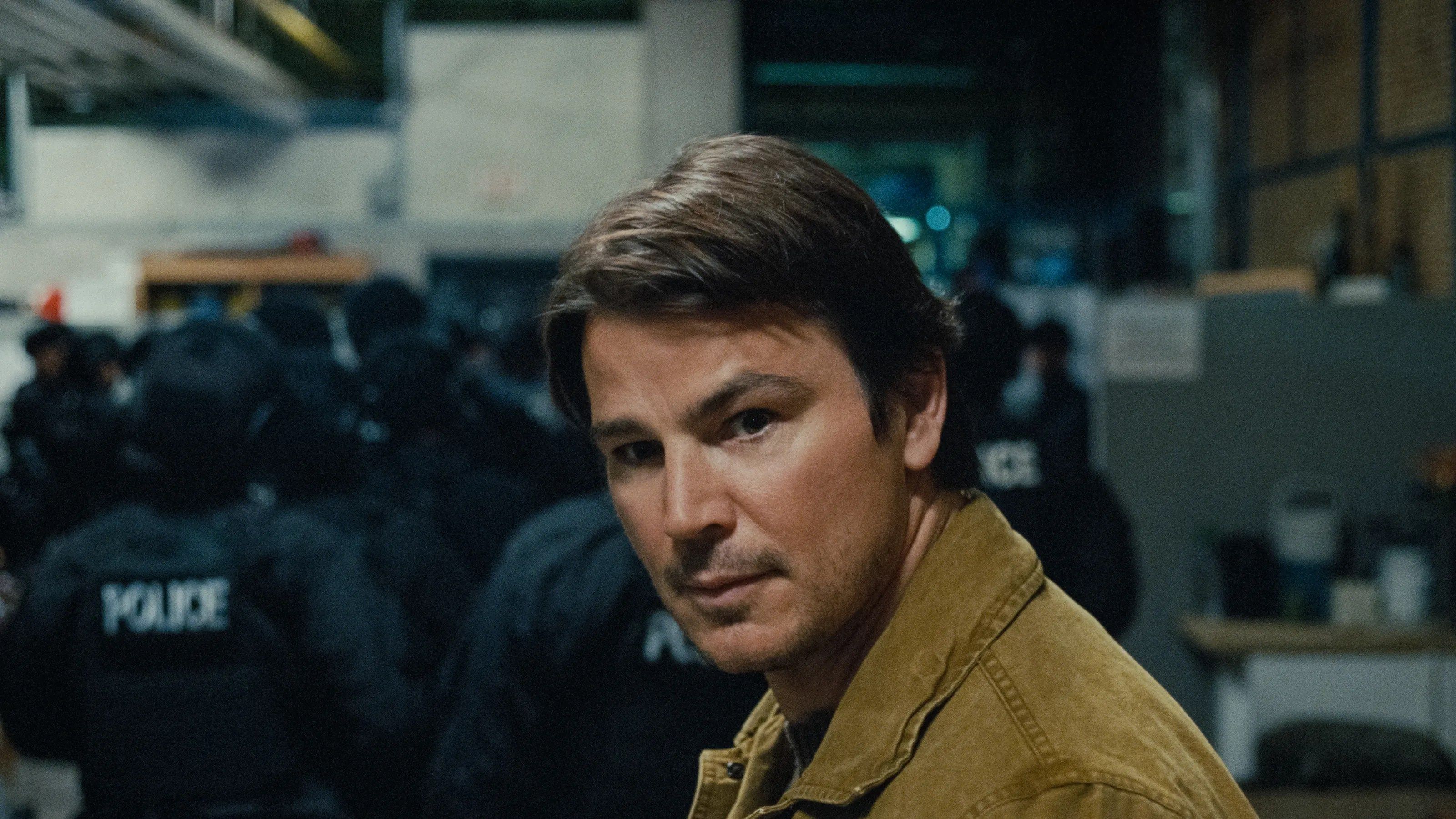 Josh Hartnett as Cooper, standing behind a room full of police officers in tactical gear, in Trap.