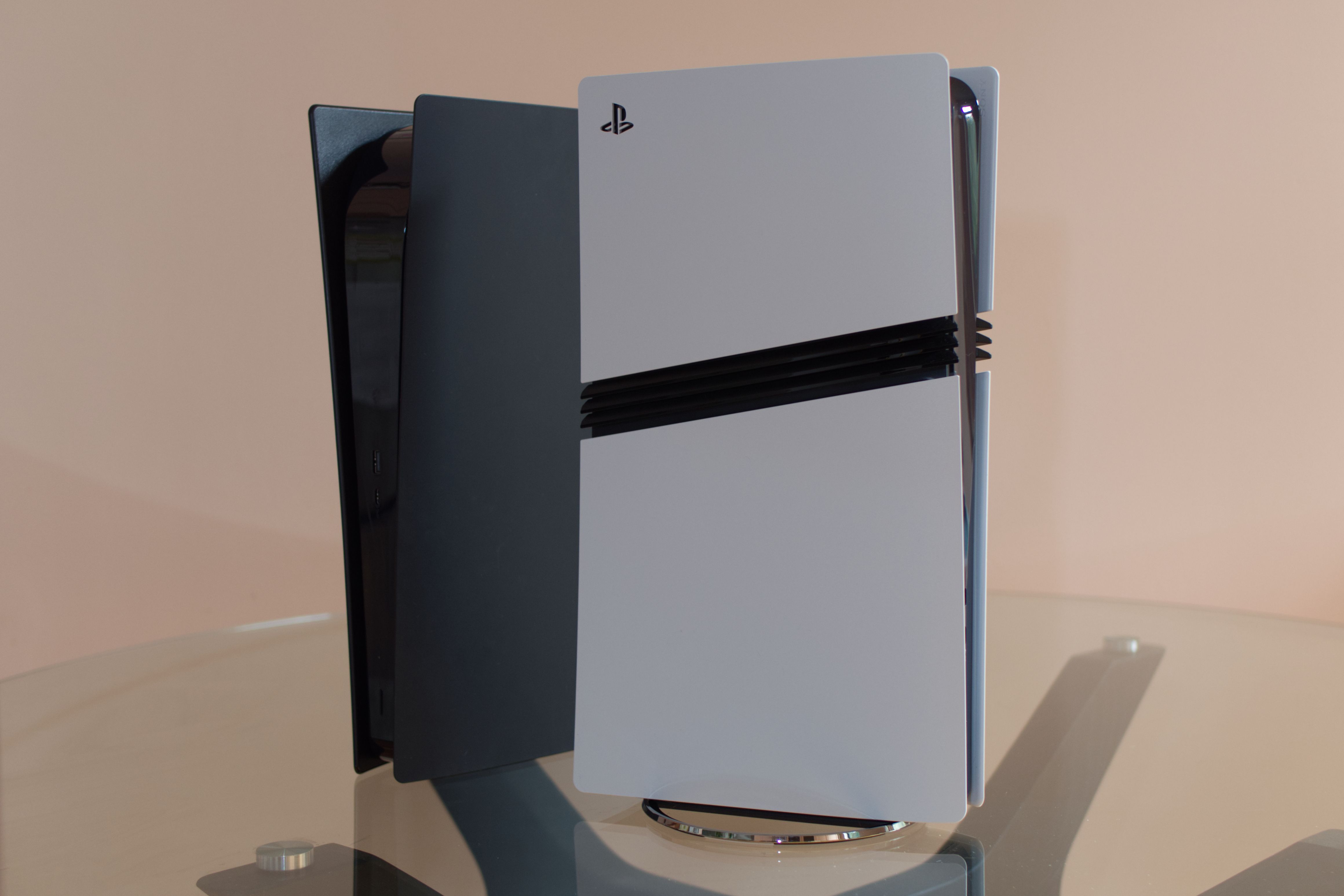 The PS5 Pro sits on a glass table next to the base PS5 console with black console plates.